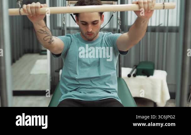 Man performing seated core exercise on pilates trapeze holding bar to ...