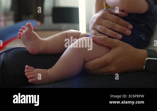 Baby cradled in mothers arms, legs resting on lap, relaxed posture ...