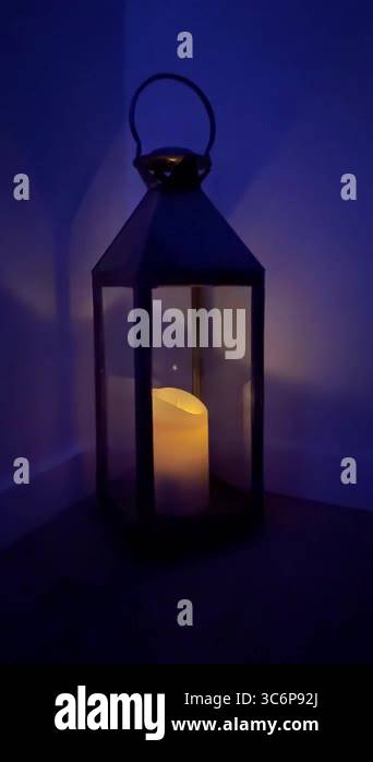 A warm candle glows inside a rustic glass lantern, casting soft shadows ...