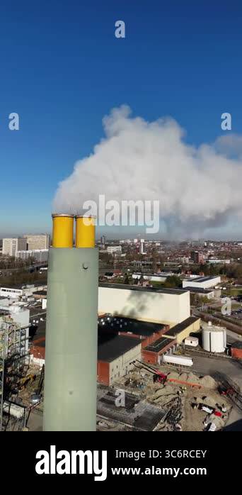 Smoke billows from a tall factory chimney against a bright blue sky ...