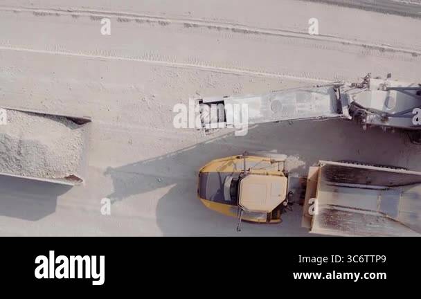Top aerial view of bulldozer loading stones into empty dump truck in open air quarry. Excavator ...