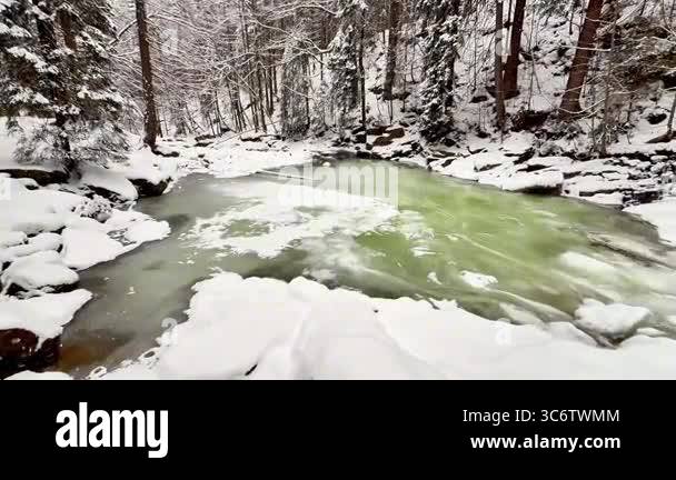 An incredibly serene winter river scene featuring snowcovered rocks and tall trees, showcasing ...