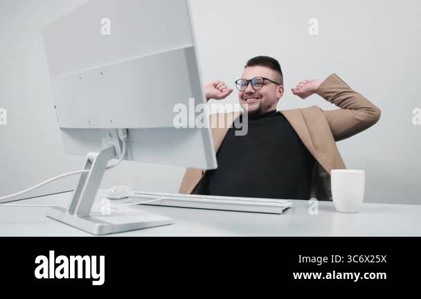 A happy young businessman in a suit looks at his computer, rejoicing at ...