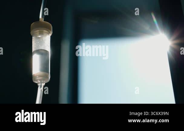 IV drip chamber illuminated by sunlight near a window, symbolizing hope ...