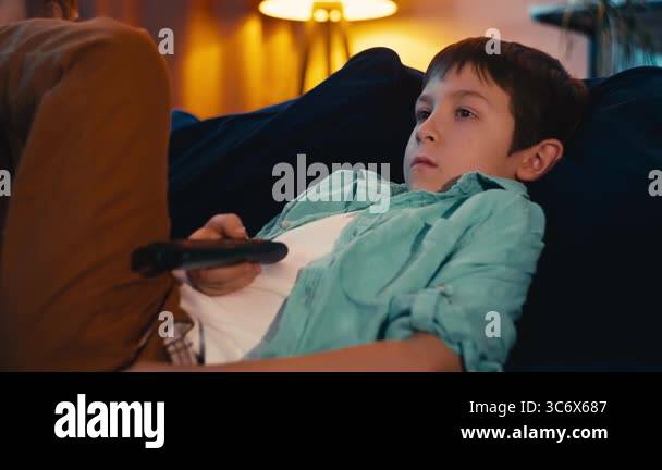 Caucasian boy switches channels with the remote control on the TV. The ...