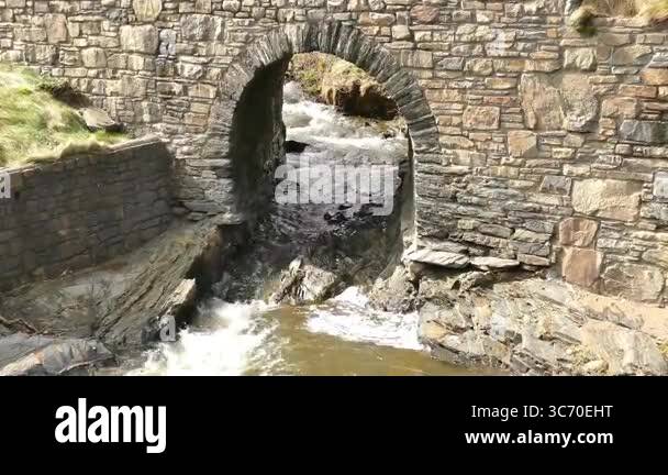 A picturesque stone arch bridge spans a rushing river in a serene ...