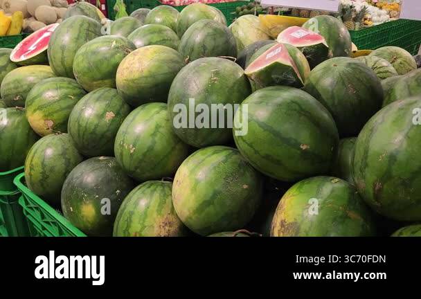 A large pile of ripe green watermelons stacked in baskets at a ...