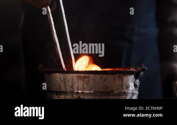 Metalworker quenching hot metal in a bucket of water, creating steam ...