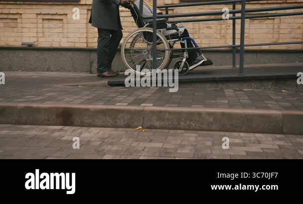 Elderly husband pushes wife in wheelchair along special ramp. Retired ...