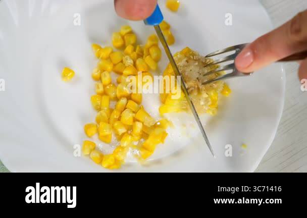 Woman cutting piece of baked corn on plate on kitchen at home, hand ...