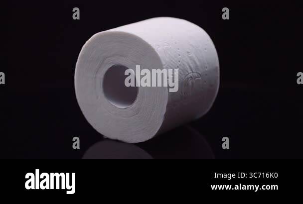 Soft white toilet paper roll rotating on dark studio backdrop in close ...