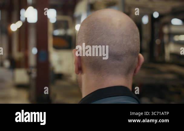 Back view tracking shot of bald male mechanic in work jacket ...