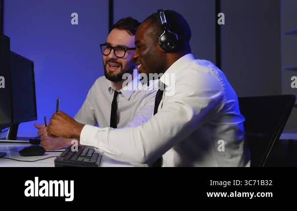 Two IT operators in a data center analyze and process large datasets on multiple monitors. They ...