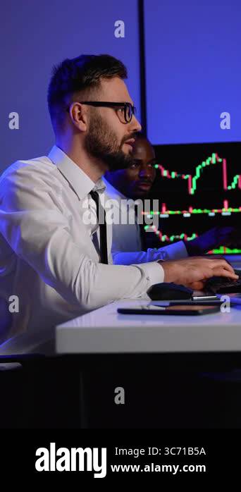 Two financial traders in a modern office analyze stock market data on multiple monitors ...