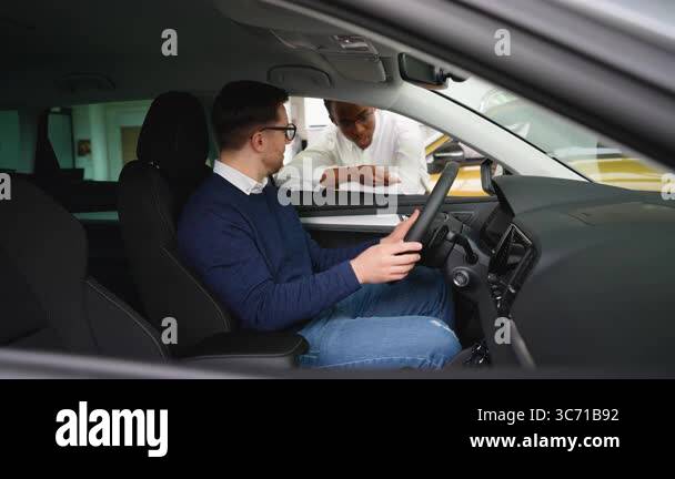 A car salesman explains the features of a vehicle to a customer sitting ...