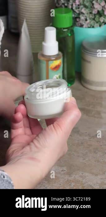 Woman in dressing gown open cap of glass jar of face cream in modern ...