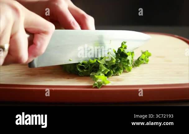 close-up of a woman's hands slicing fresh lettuce on a wooden cutting ...