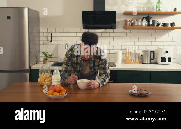 Young African American man standing at the kitchen counter, eating ...