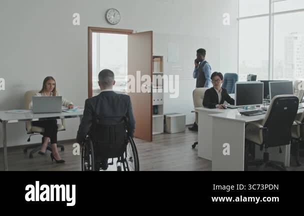 Slowmo tracking shot of male executive in wheelchair being greeted by ...