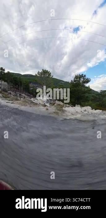 Vertical video. red car driving on a narrow dirt road encircled by ...