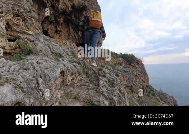 Woman with Yellow Backpack Walking Along Rocky Cliff Path Overlooking ...