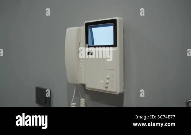 Wall-Mounted White Intercom With A Small Blue Screen, Coiled Cable, And ...