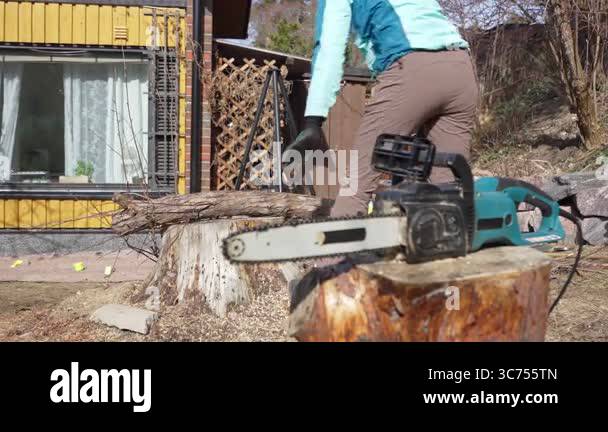 A strong, confident woman operates an electric chainsaw, sawing through ...
