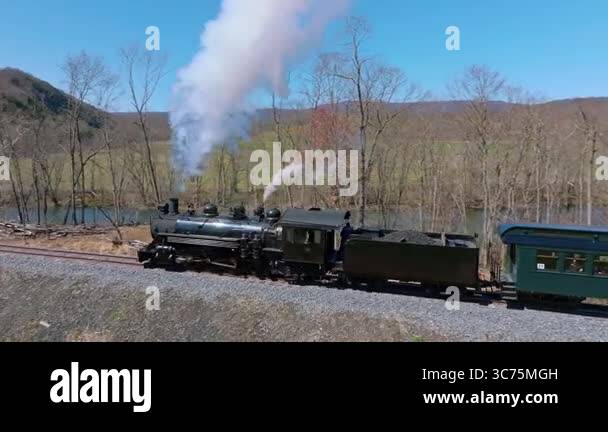 A classic steam locomotive steams down the tracks alongside a peaceful ...