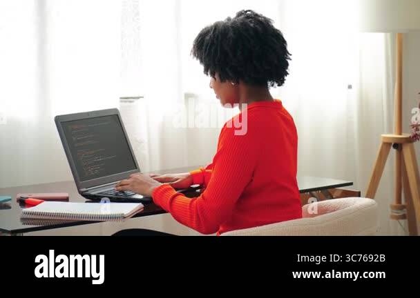 A cheerful young woman engaged in coding on her laptop, demonstrating her passion for ...