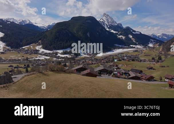 Aerial view of Gstaad village cityscape and Wispile mountain showing late winter snow melting in ...