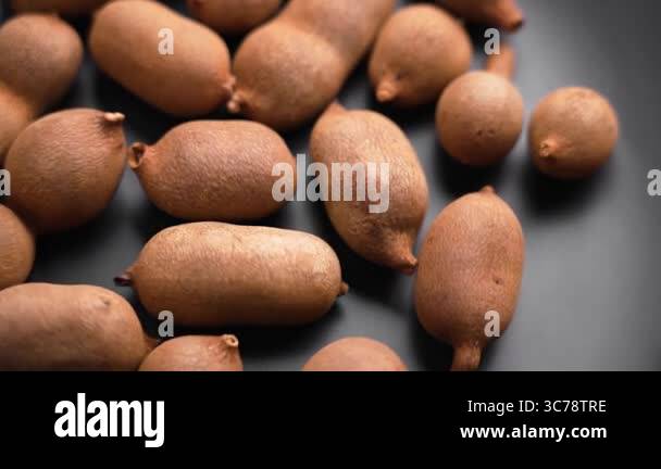 Shaking fresh tamarind fruits in shells on a black ceramic plate. Macro ...