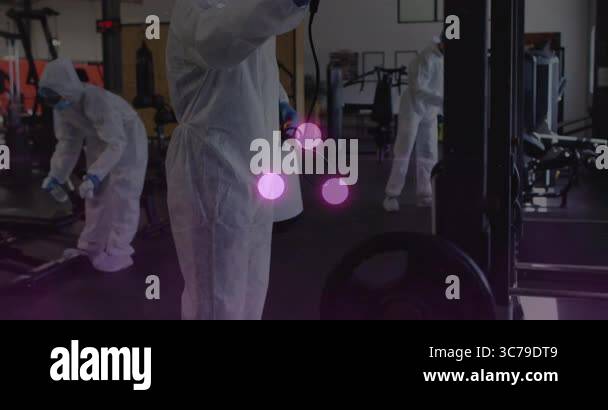 People in protective suits disinfecting gym equipment with glowing ...