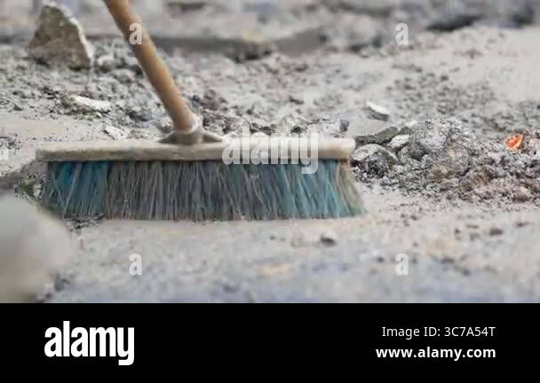 A worker sweeps dust and debris from a construction site during daytime ...
