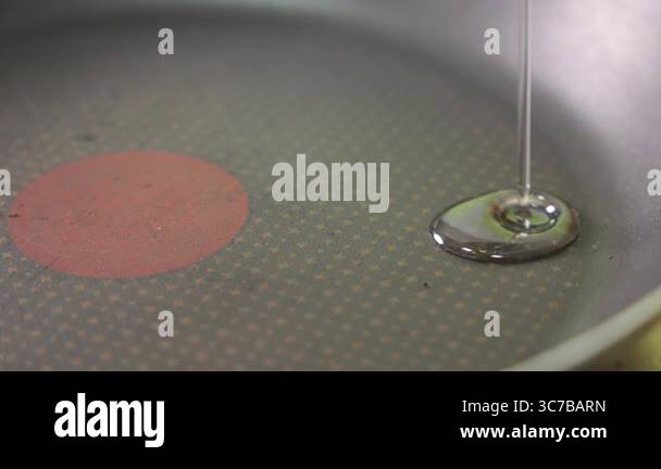 A stream of oil being poured into a non-stick frying pan with a red ...