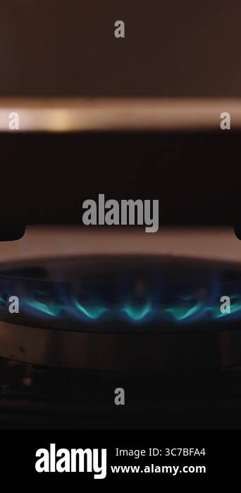 Vertical video. Blue Gas Flames Heating a Nonstick Pan with a Silicone Spatula in the Background ...