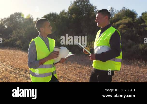 Two engineers wearing high visibility vests review project plans in a ...