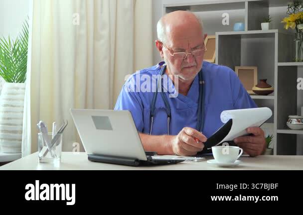An elderly male doctor, practicing medicine, working with documents ...