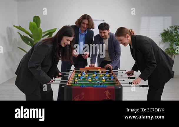 A group of colleagues in formal attire enjoy a lively game of foosball ...