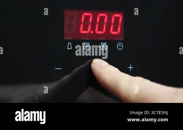 Close-up of a hand adjusting the digital display of a microwave oven ...