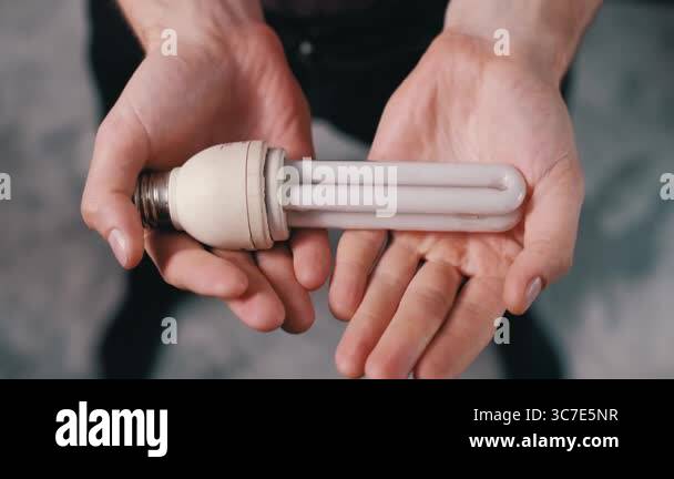 A man closely examines a white compact fluorescent lamp CFL in his ...