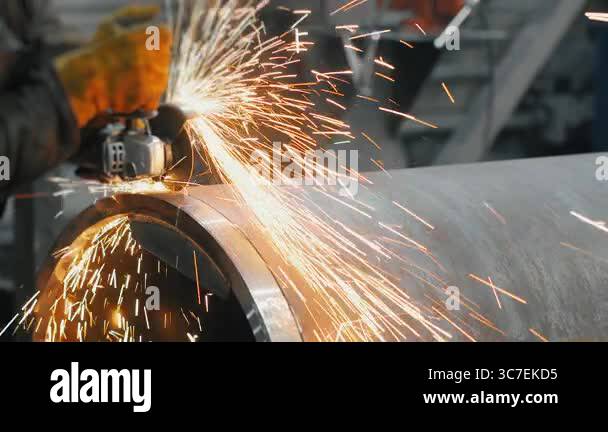 A worker at a metalworking plant processes a large pipe with a grinder ...