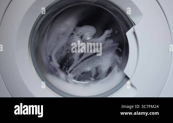 Inside a washing machine, clothes spin in soapy water. Closeup view ...