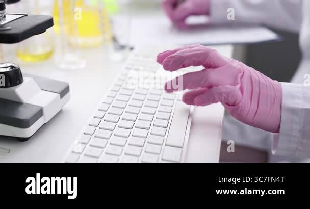 Laboratory technician sits at desk and types on computer keyboard ...