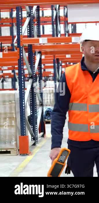 Warehouse worker wearing safety vest and hardhat walking through ...
