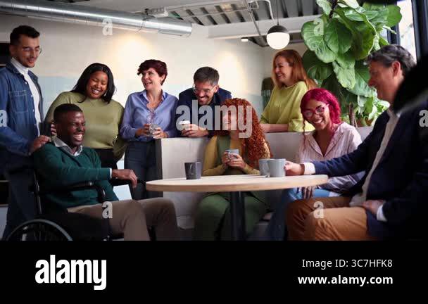 Office workers gather around a colleague in a wheelchair, enjoying a ...
