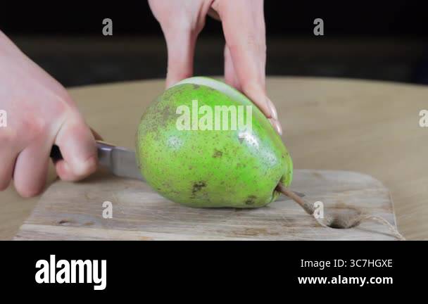 Sliced green pear with visible rot inside, held by hand on a wooden ...