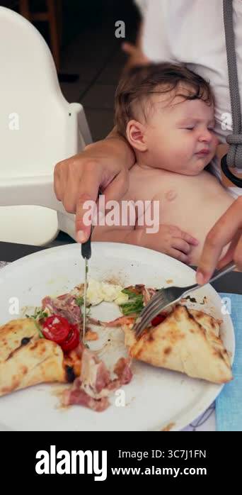 Mother eating meal while holding baby, multitasking with fork and knife ...