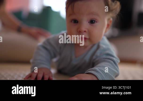 Baby lying on mat indoors, lifting head with curious expression ...