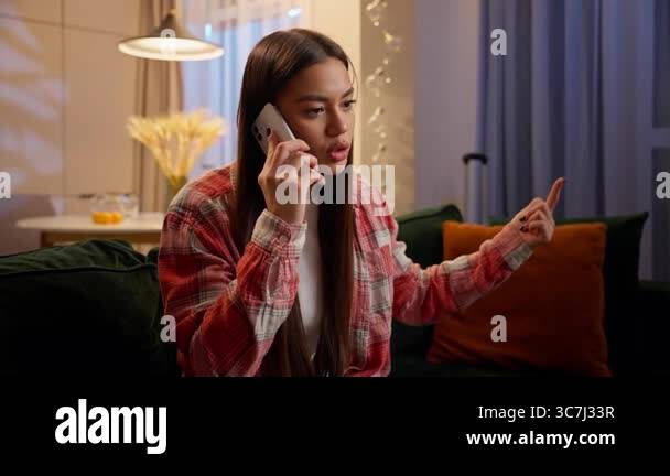 Angry Caucasian woman teen girl mad furious talking mobile phone at home night call female ...