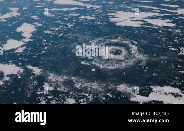 A close-up of a frozen lake with a hole in the ice, surrounded by frost ...